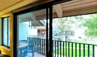 Varanda com mesa e cadeiras, vista para uma área residencial com casas e árvores.