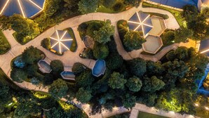 Vista aérea de uma área ajardinada com caminhos, espaços para sentar e estruturas iluminadas.