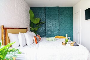 Quarto com parede de tijolos brancos, cabeceira de madeira e cama com roupa de cama branca.