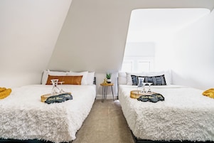 Quarto com duas camas, uma mesinha de cabeceira com uma planta e uma janela.