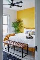 Quarto com cama, um banco, ventilador de teto e janela.