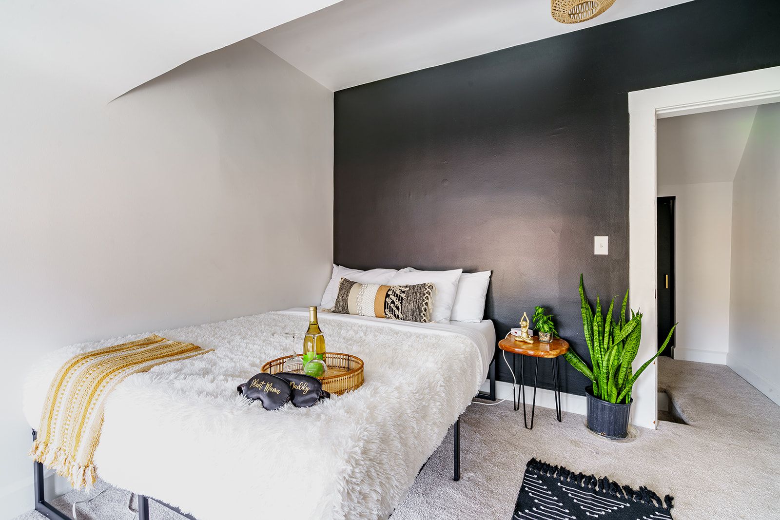Quarto moderno com cama, mesas de cabeceira, uma planta e uma porta.
