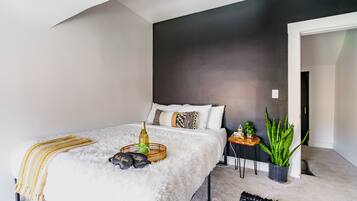 Quarto moderno com cama, mesas de cabeceira, uma planta e uma porta.
