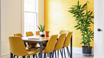 Uma área de refeições com mesa, cadeiras, uma planta em vaso e uma parede de tijolos amarelos.