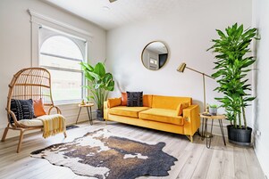 Sala de estar com sofá, uma poltrona, um espelho grande e plantas em vasos.