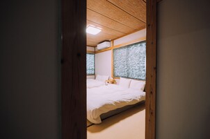 Quarto com uma cama, uma pequena mesa de cabeceira de madeira, uma janela com persianas e um ar condicionado no teto.