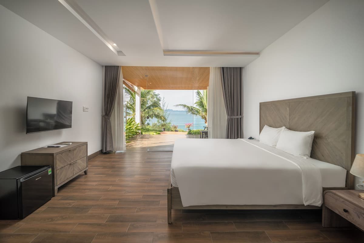 Quarto de hotel com cama, televisão, mini-frigorífico e vista para o oceano.