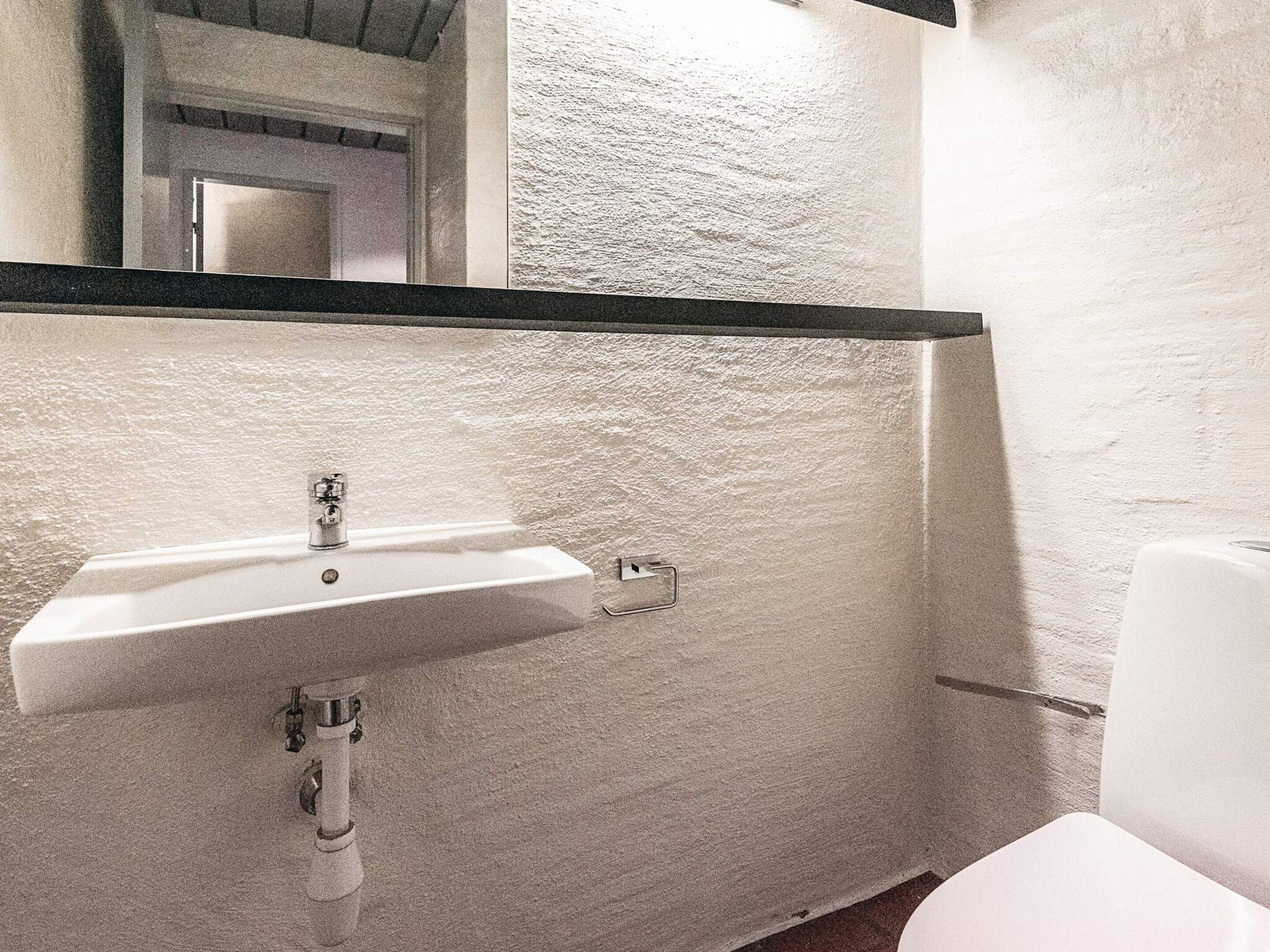 Casa de banho com lavatório branco, espelho e sanita.