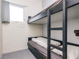 Quarto com beliche, janela, tomadas na parede e piso coberto por carpete.