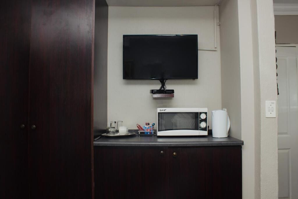 Uma pequena cozinha compacta com micro-ondas, máquina de café e televisão de tela plana fixada na parede.