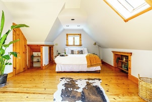 Quarto com teto inclinado, uma cama grande, claraboia, piso de madeira e tapete de couro.