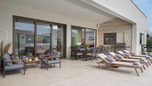 Uma área externa moderna com mesa de jantar, cadeiras, poltronas de descanso e churrasqueira.
