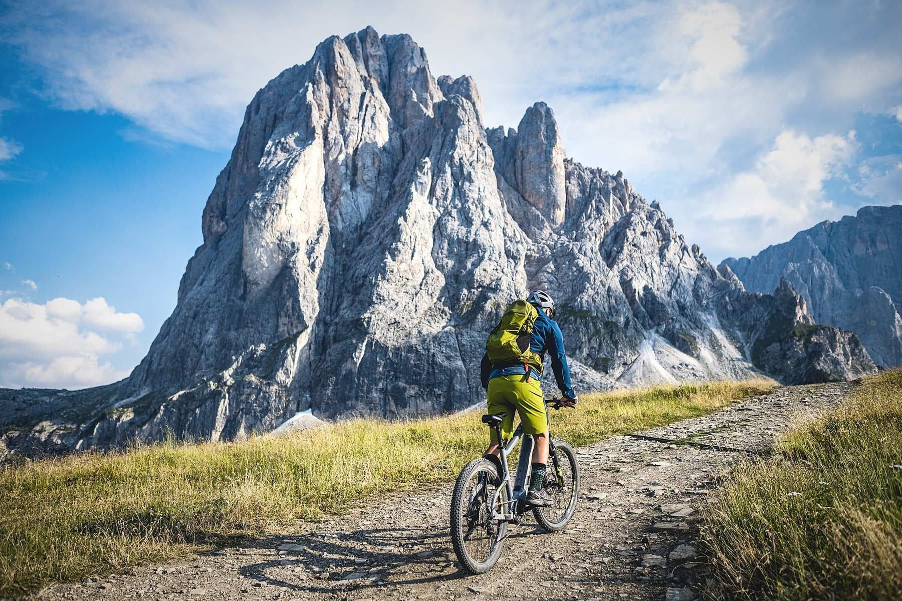 Ciclista de montanha numa trilha de terra, com uma montanha rochosa ao fundo.