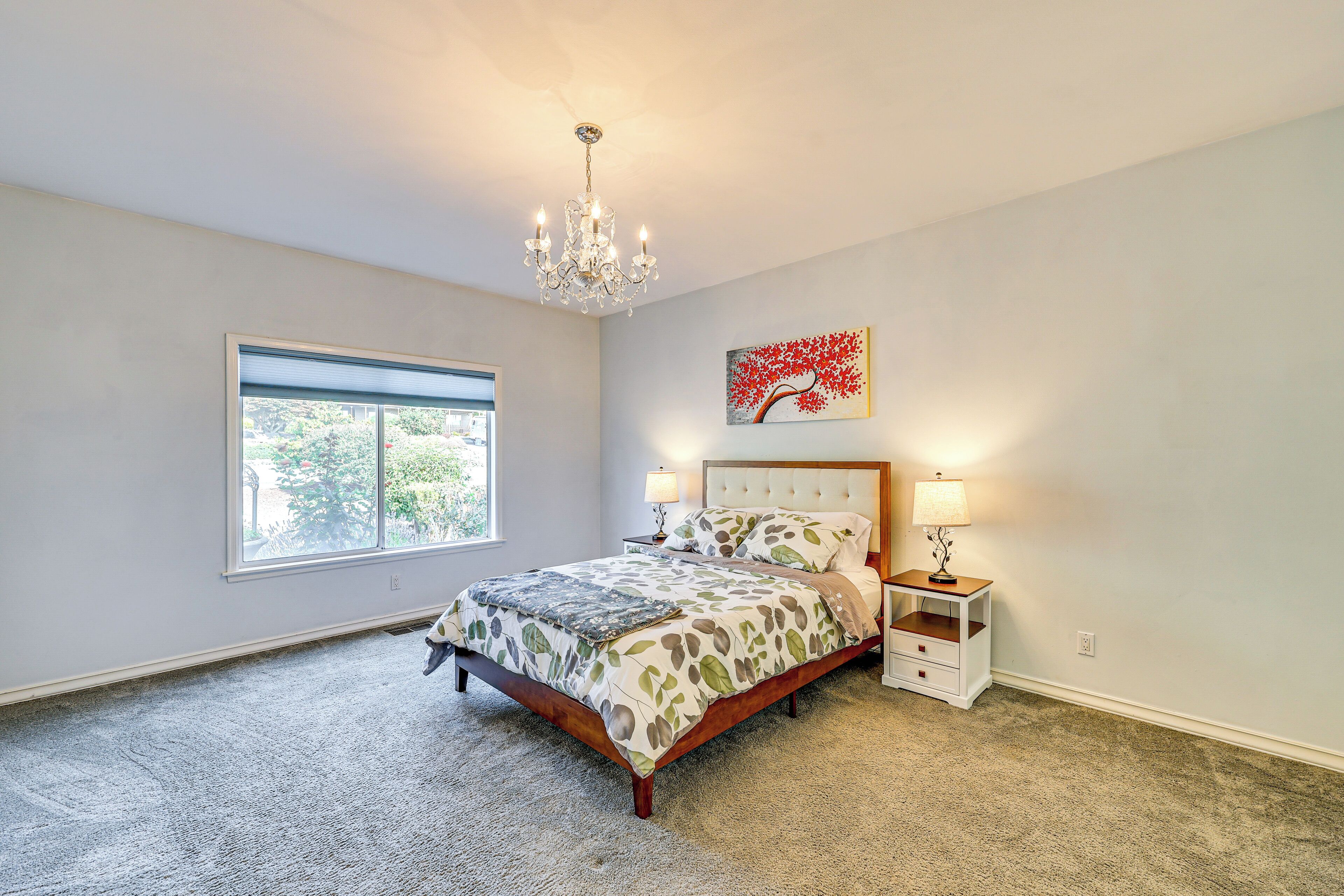 Quarto com uma cama grande, um candelabro, uma janela e uma mesa de cabeceira com abajur.