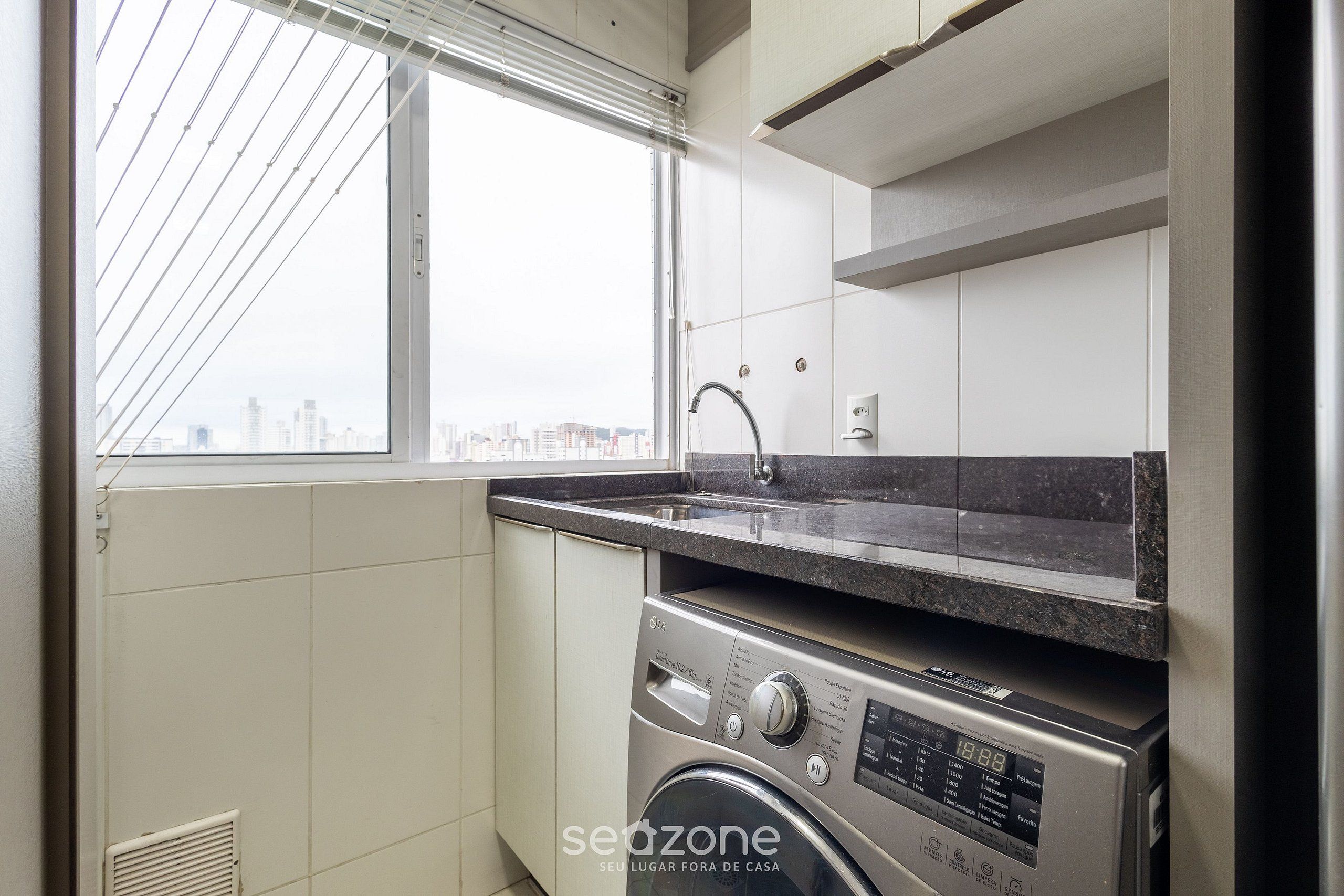 Uma cozinha compacta com máquina de lavar e secar integradas, uma janela com persianas e vista para o horizonte urbano.