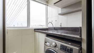 Uma cozinha compacta com máquina de lavar e secar integradas, uma janela com persianas e vista para o horizonte urbano.