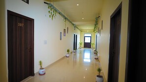 Um corredor com portas de madeira numeradas 107 e 102, plantas em vasos e quadros nas paredes.