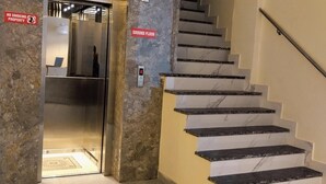 Um elevador com um aviso de 'PROIBIDO FUMAR', um aviso de 'PISO TÉRREO' e um vão de escadas com degraus de mármore.
