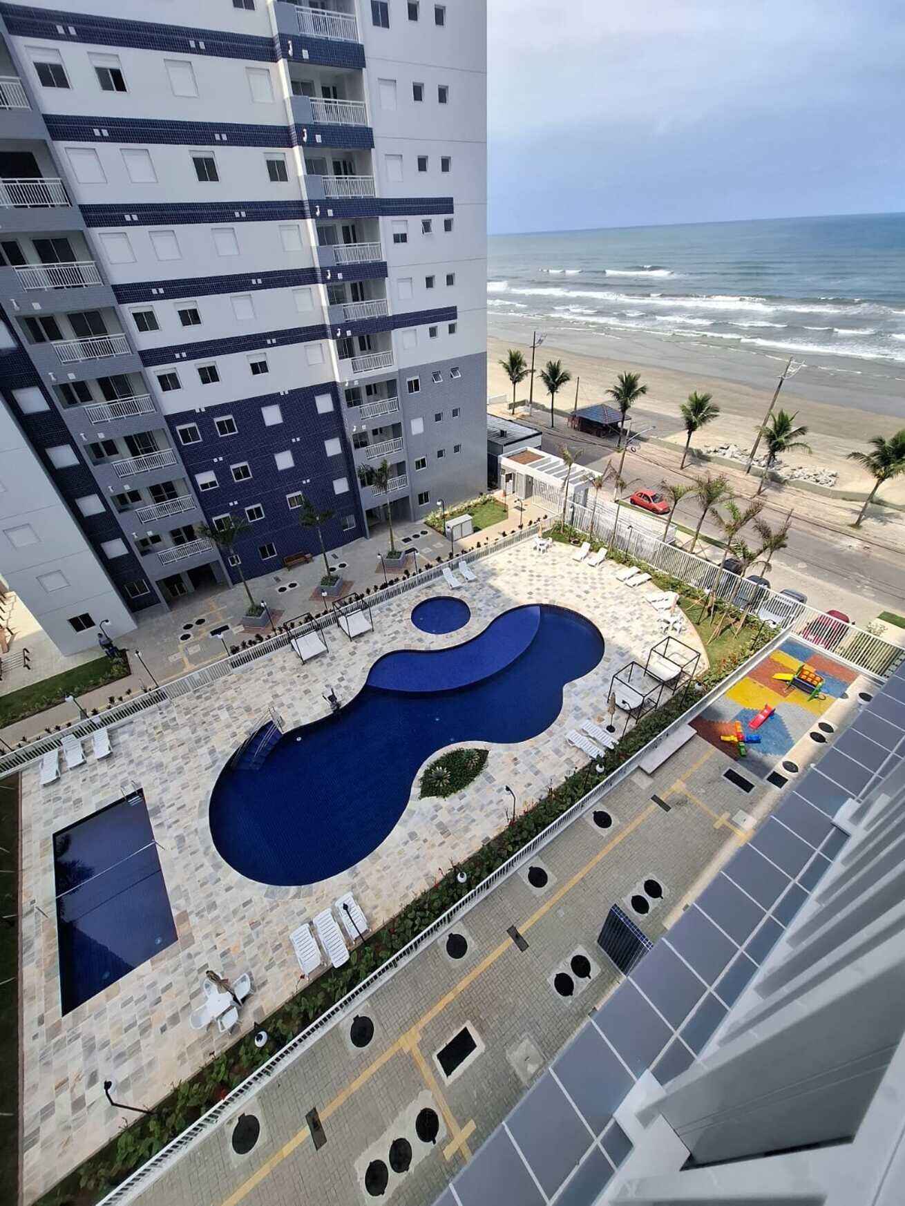 Um hotel alto com piscina no terraço, vista para a praia e área de estacionamento.