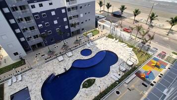 Um hotel alto com piscina no terraço, vista para a praia e área de estacionamento.