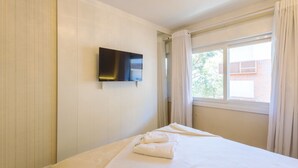 Quarto de hotel com cama, televisão de tela plana na parede e janela com cortinas.