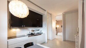 Cozinha moderna com armários escuros, bancada branca e luminária pendente. Há uma mesa de jantar com cadeiras e uma pia visível.
