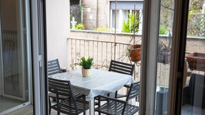 Varanda com mesa, cadeiras, planta em vaso e vista para um edifício e vegetação.
