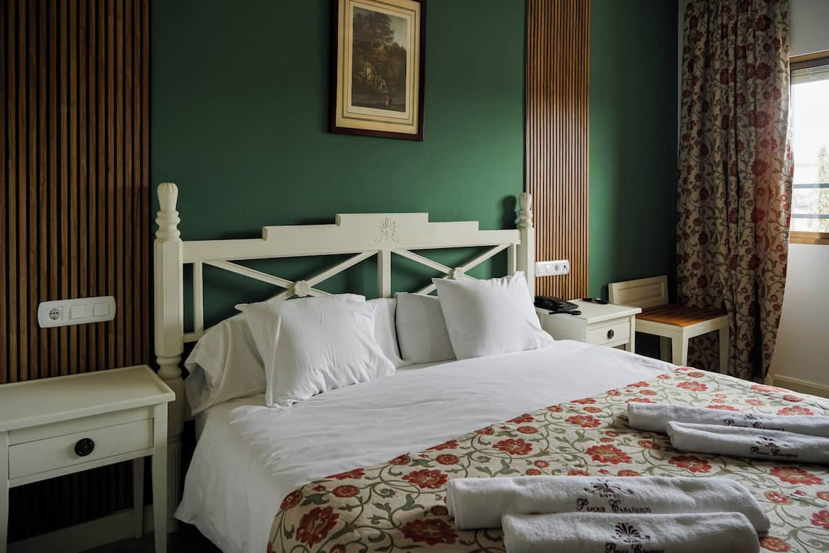 Cama bem arrumada com lençóis brancos, um espalha-cama estampado com flores e toalhas dobradas na cama.