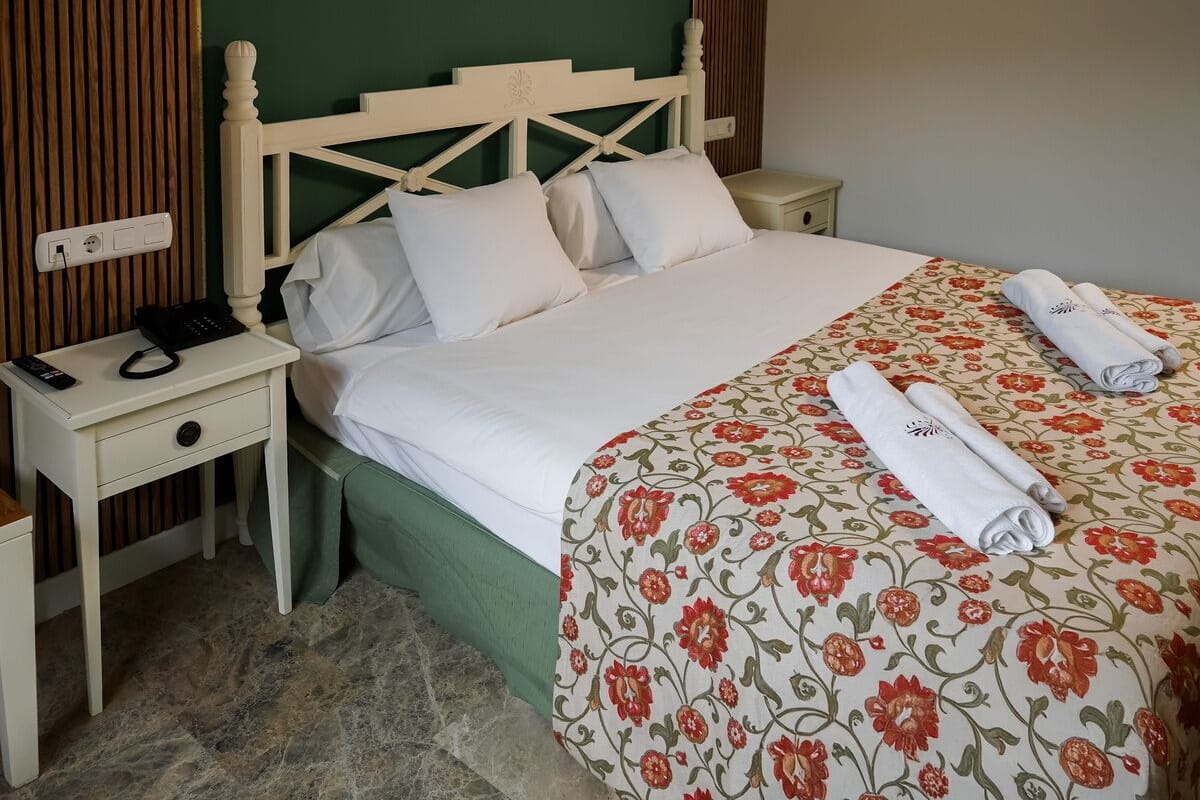 Quarto de hotel com uma cama, mesa de cabeceira com telefone e tomada elétrica.
