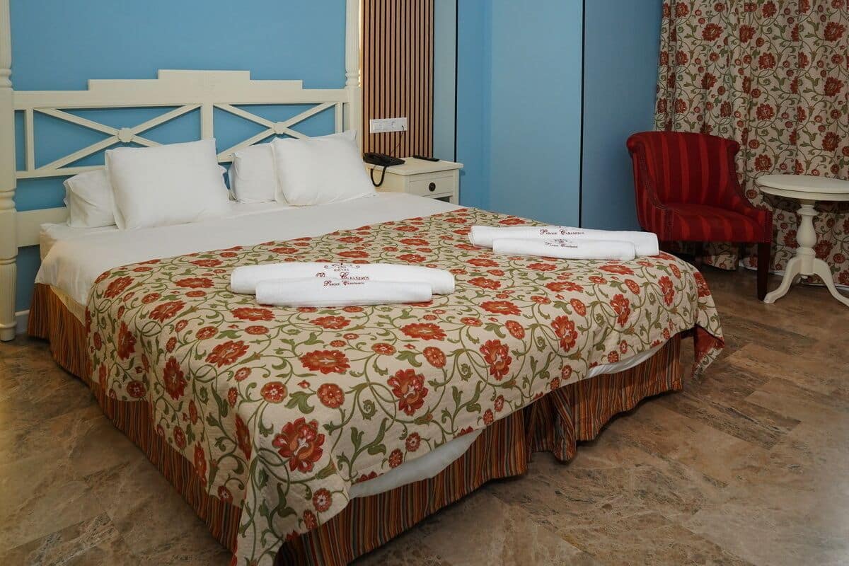 Quarto de hotel com uma cama, mesa de cabeceira, uma cadeira vermelha e uma pequena mesa.