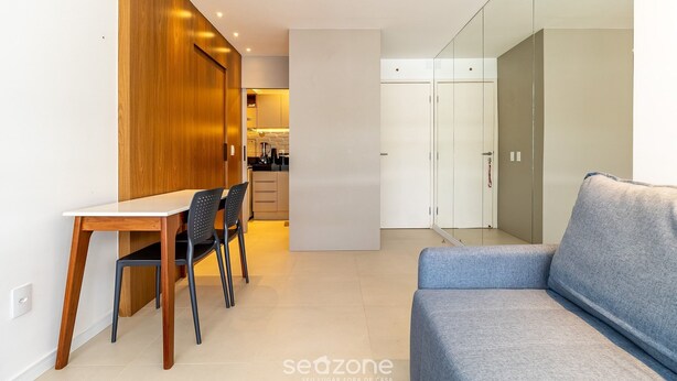 Uma sala de estar moderna com sofá, mesa de jantar e cadeiras, e área de cozinha ao fundo.
