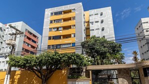 Um edifício residencial de vários andares, com varandas, fachada amarela e um muro de pedra com portão.
