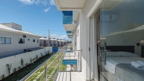Quarto de hotel com varanda e vista para uma piscina e edifícios vizinhos.