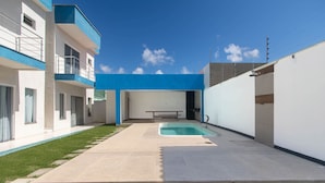 Um edifício moderno com piscina, um alpendre coberto e uma área gramada.