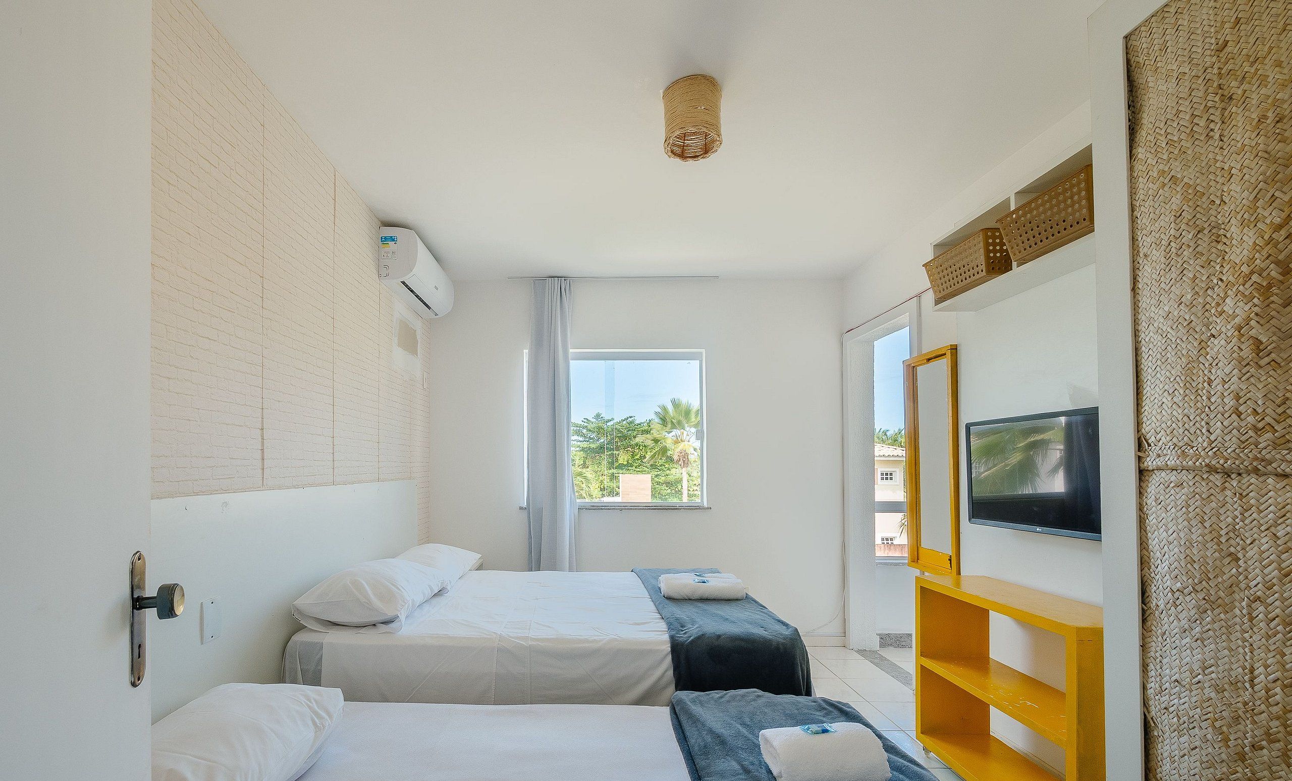 Quarto de hotel com duas camas, uma televisão na parede e janela com vista para áreas verdes.