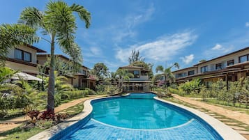 Piscina rodeada por palmeiras e um céu azul límpido.