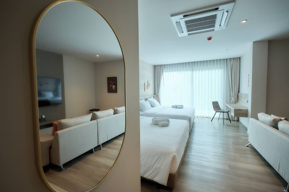 Quarto de hotel com um espelho grande, televisão de tela plana, duas camas, um sofá, uma escrivaninha e uma cadeira.