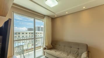 Uma sala de estar moderna com um sofá, uma mesinha e uma cadeira. Há uma janela grande com vista para edifícios.