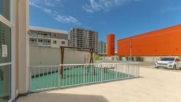 Um edifício residencial com área externa cercada, piscina e um grande edifício industrial laranja ao fundo.