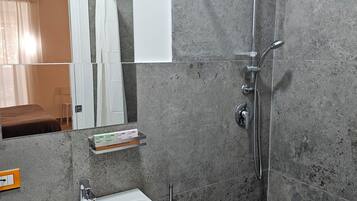 Uma casa de banho moderna com chuveiro, lavatório e espelho.