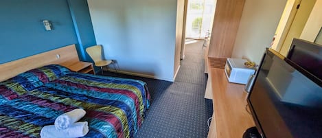 Quarto de hotel com cama, escrivaninha, televisão e uma cadeira.