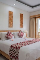 Quarto de hotel com uma cama grande, painéis decorativos na parede, uma mesa de cabeceira com abajur e vista para o exterior através de uma janela com cortinas.
