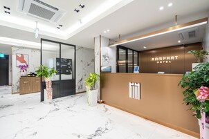 Uma área de recepção de hotel moderna, com piso de mármore, balcão de atendimento e plantas em vasos.