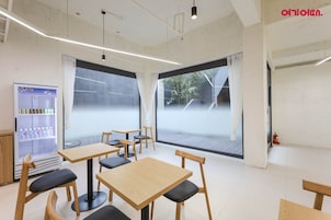 Interior moderno de café com mesas e cadeiras de madeira, uma máquina de venda automática e grandes janelas com vista para o exterior.