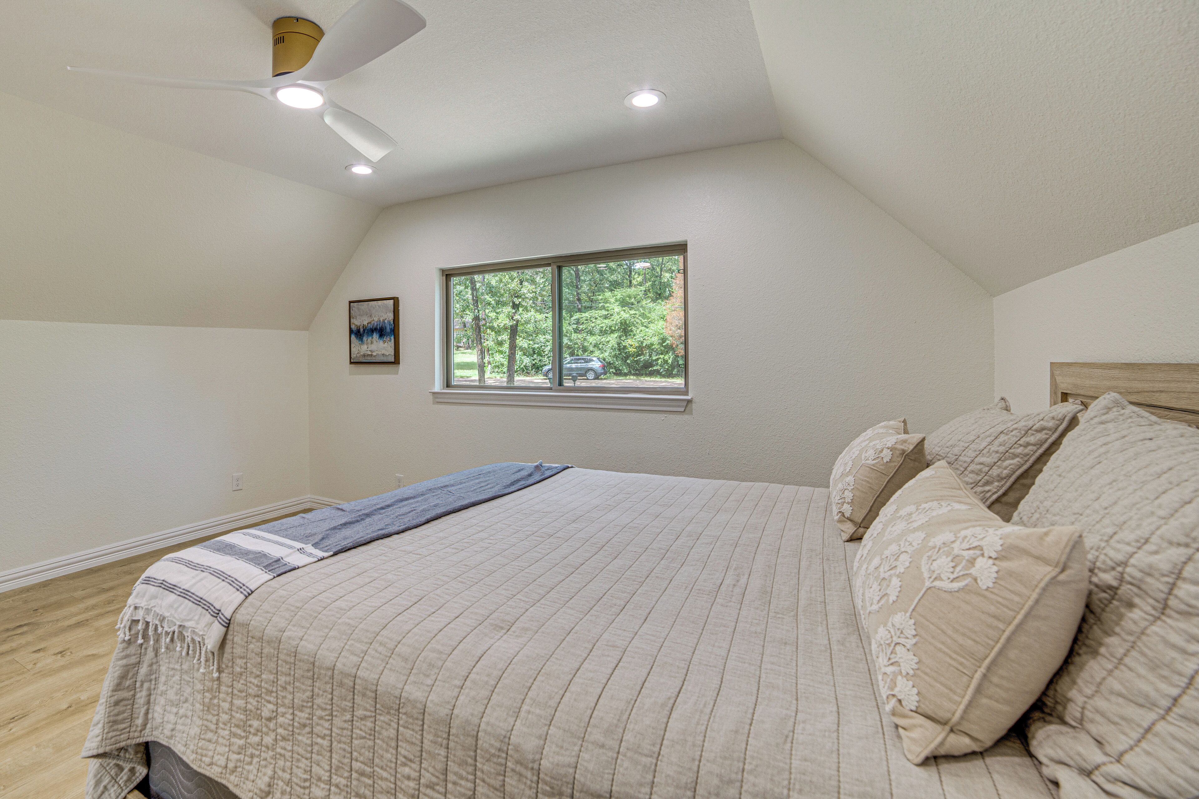Quarto com cama, janela, ventilador de teto e um quadro na parede.
