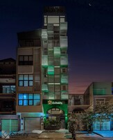 Um hotel com fachada moderna, várias varandas e uma entrada destacada com arco verde.