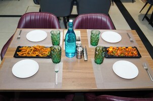 Uma mesa de jantar posta com dois pratos, dois copos, uma garrafa e duas travessas de comida.