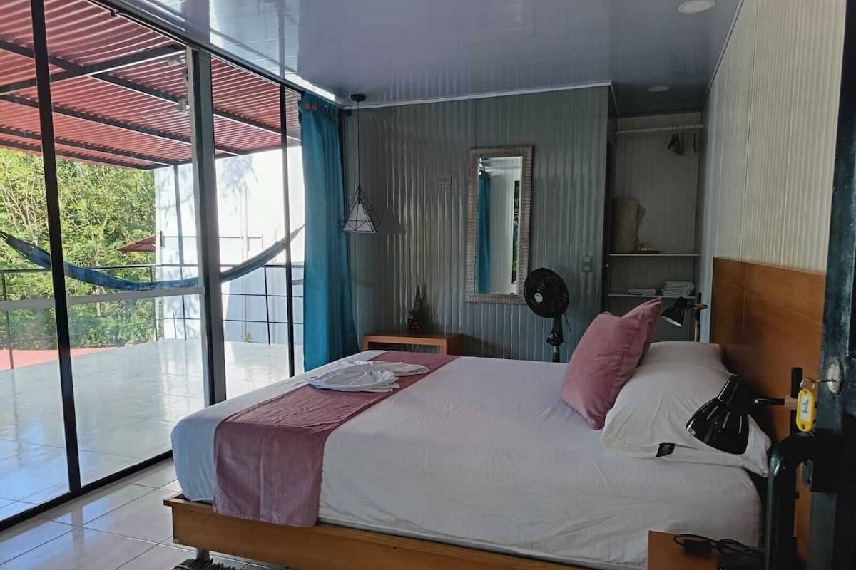 Quarto moderno com uma cama grande, um ventilador de teto, um espelho e vista para o exterior.