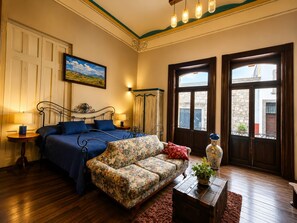 Quarto com cama, sofá, cômoda e janela com vista para edifícios.