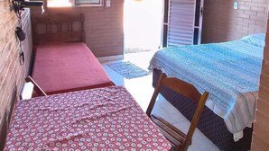 Quarto com duas camas, uma mesa e uma cadeira. Há janelas e um ventilador de teto.
